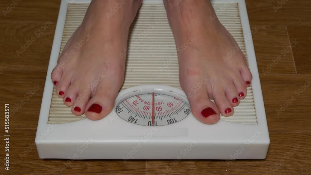 A young beautiful girl is weighed on floor scales. The girl stands with ...