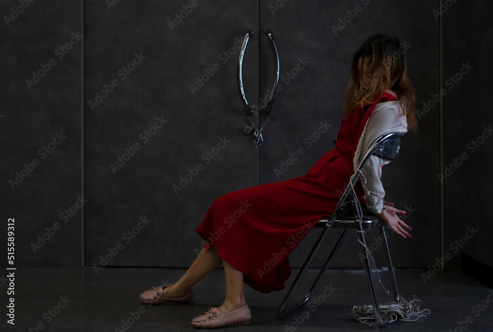 unconscious hostage woman was being hands tied behind back on chair in dark room(selective focus ...