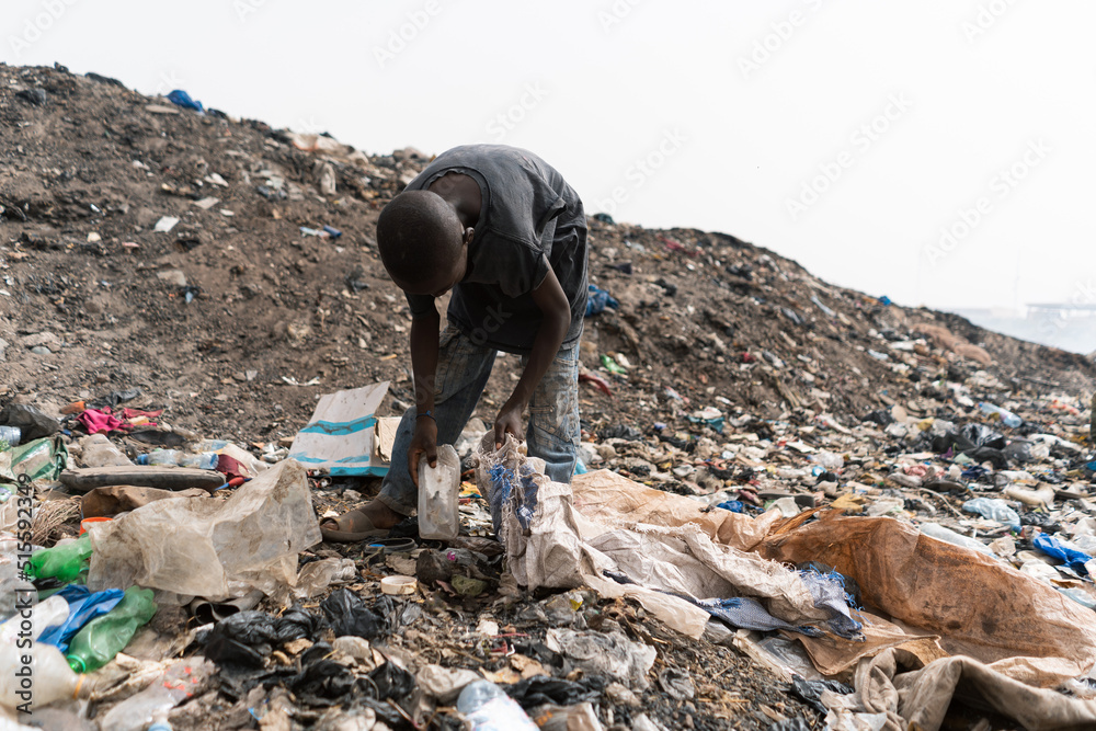Unrecognizable adolescent in a worn black T-shirt and tattered trousers ...