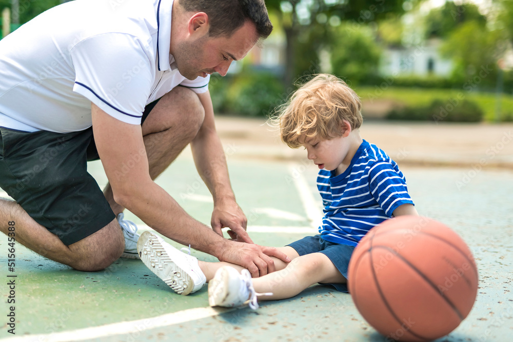 portrait of focused adult man coach helping boy with knee trauma after ...