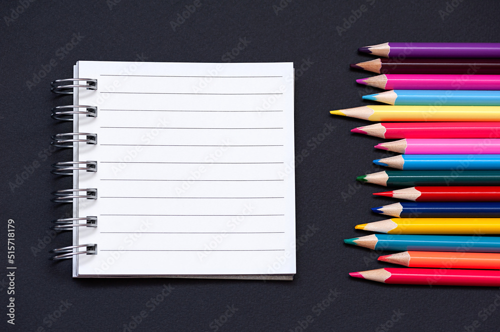 School background. Blank notepad and colored pencils on black ...