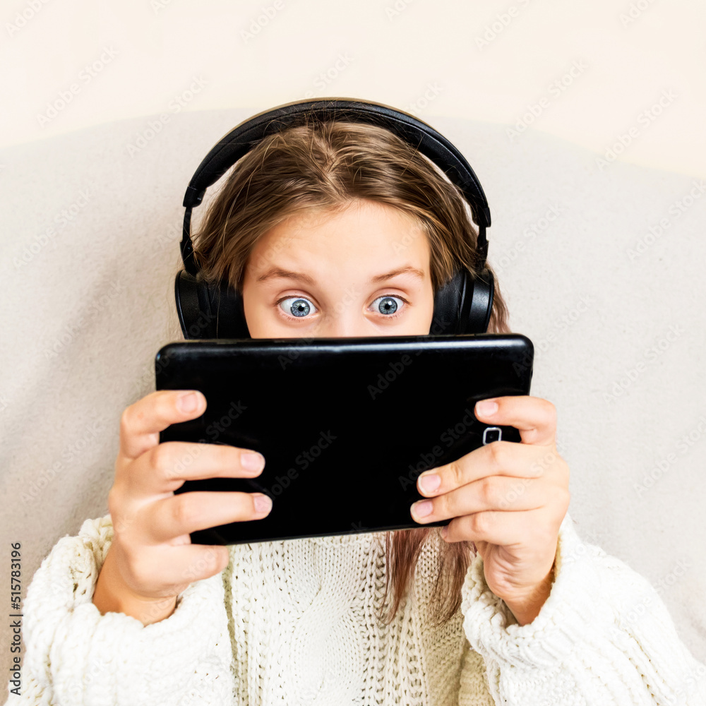 child girl sits on a sofa in wireless headphones and looks into a ...