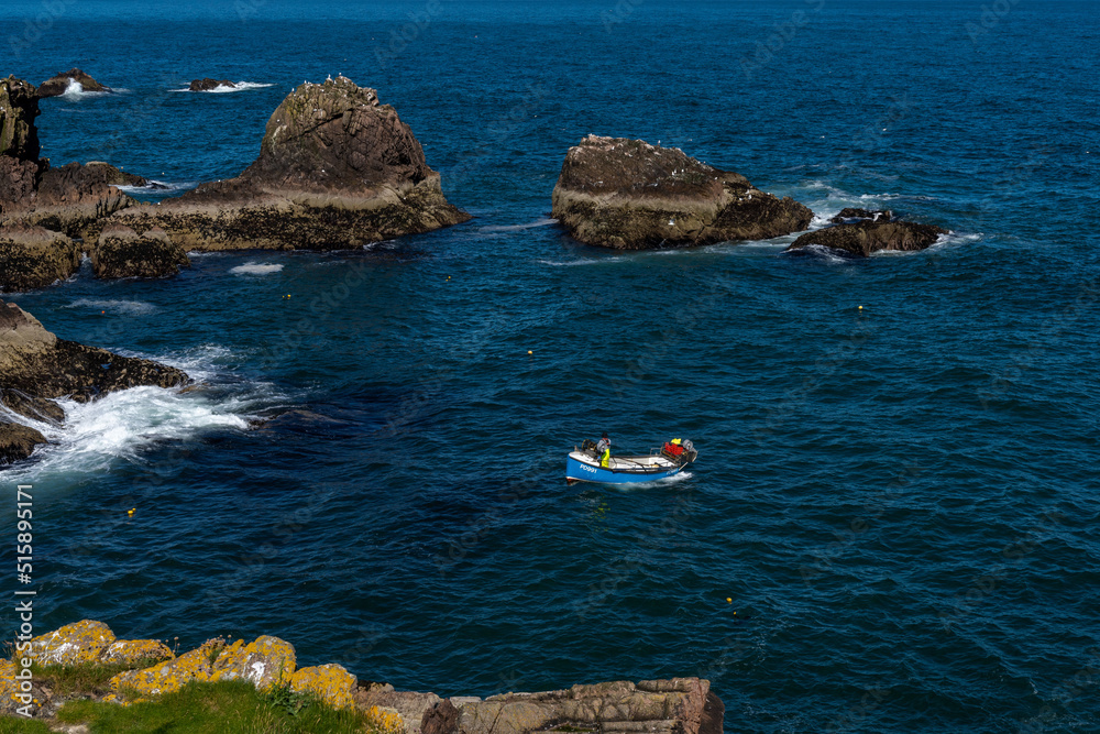 Foto de fisherman in a small wooden boat checking on his lobster pots ...
