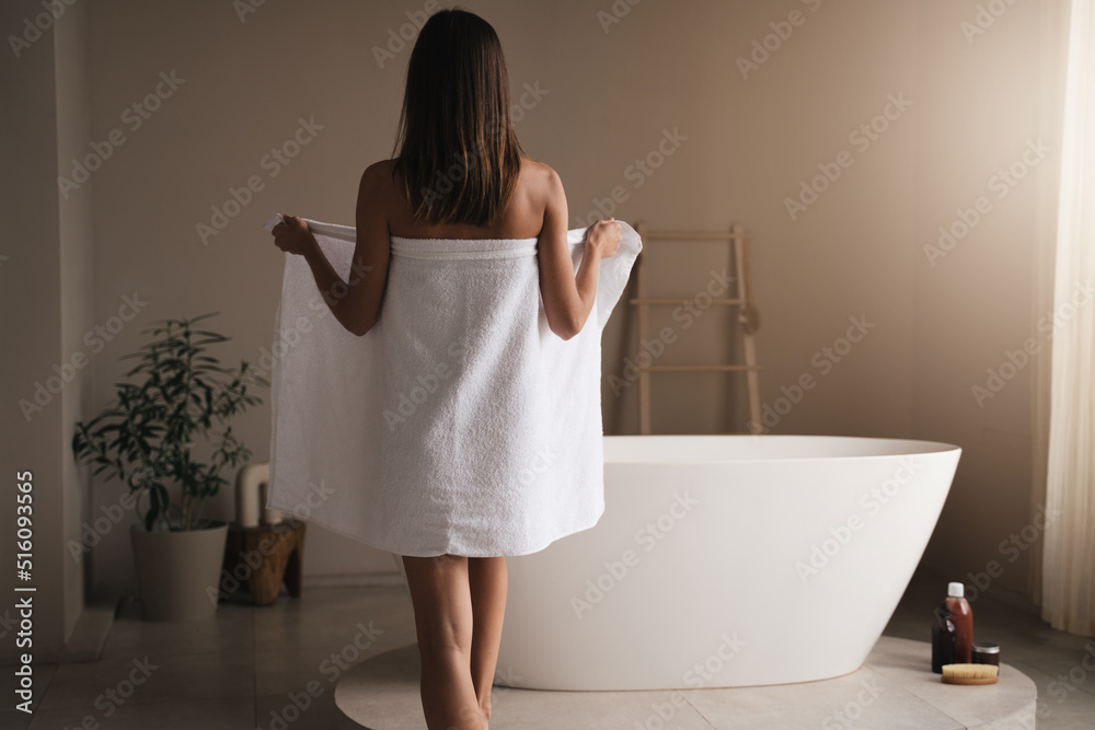 Rare view of woman taking off white towel to take bath standing next to ...