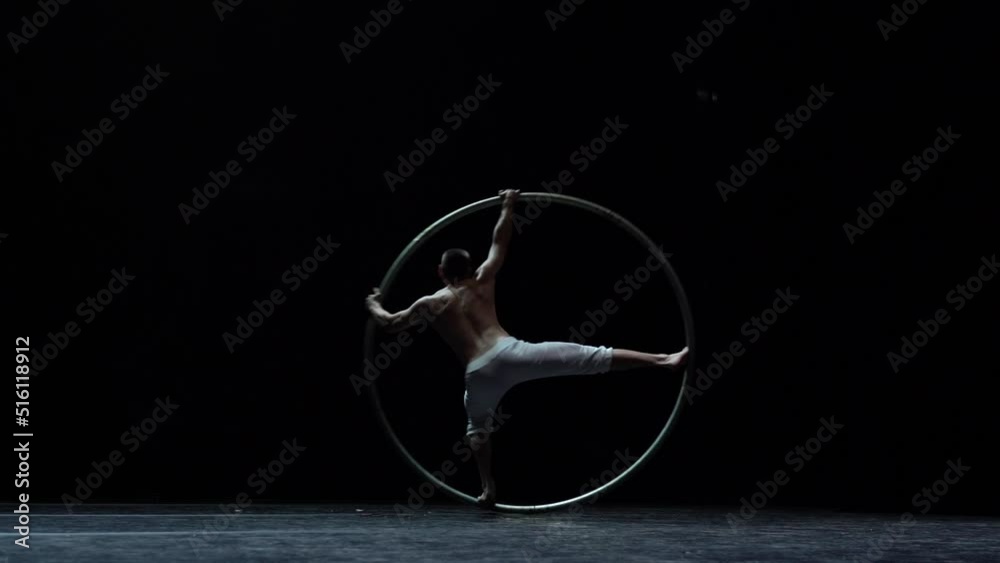 Muscular circus artist perform Cyr Wheel on a black background. Concept ...