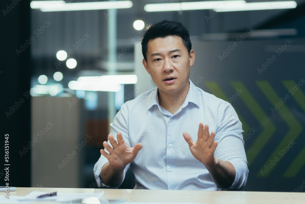 Foto de Angry asian businessman talking on video call online meeting ...