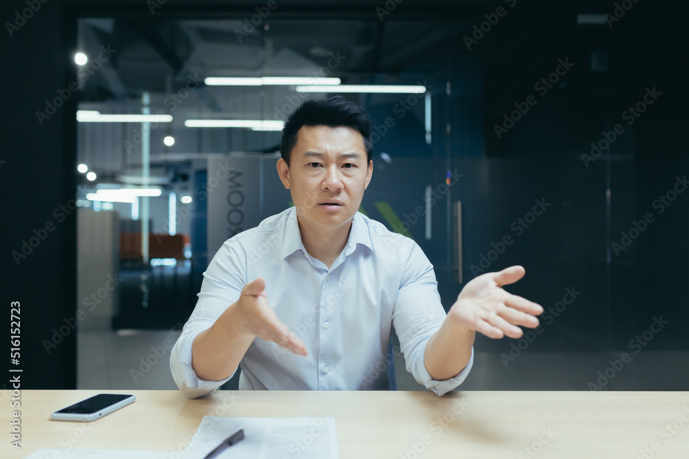 Angry asian businessman talking on video call online meeting, looking ...
