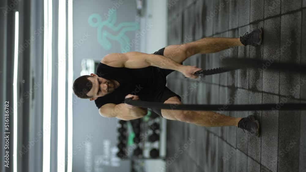 Attractive muscular man working out in the gym using battle ropes with ...