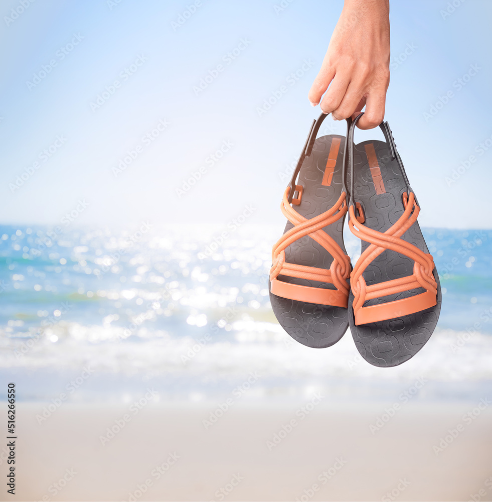 Close up woman holding flip flop on blur sand beach,blue sea and blue ...
