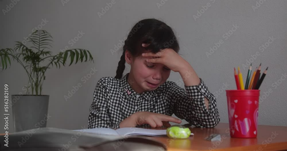 Schoolgirl in a plaid dress sits at a table in a classroom crying ...