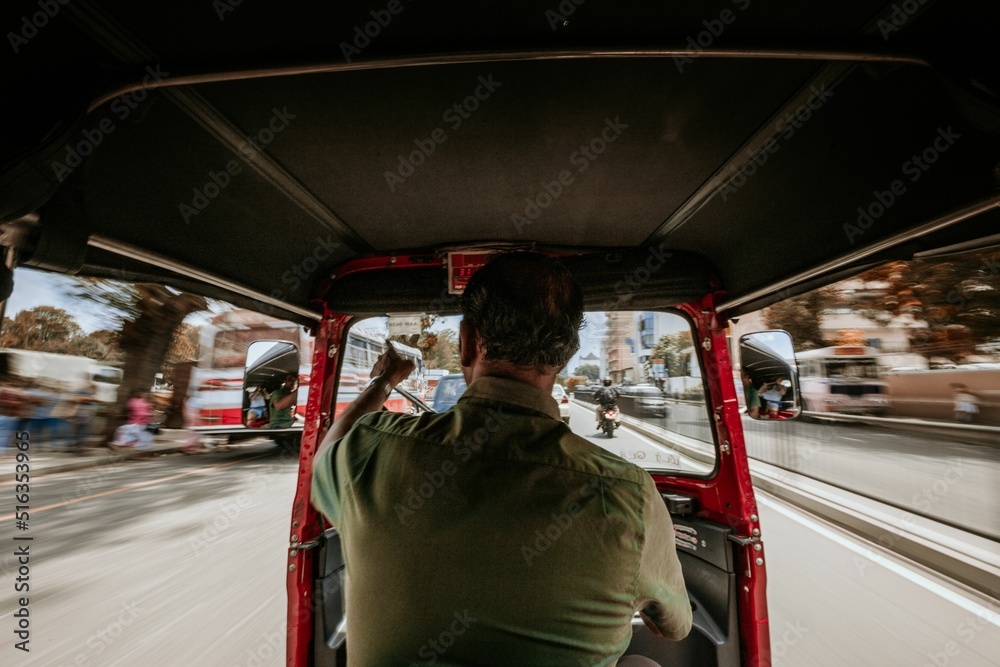 Back view of a male riding a Tuk Tuk in long exposure street of Kandy ...