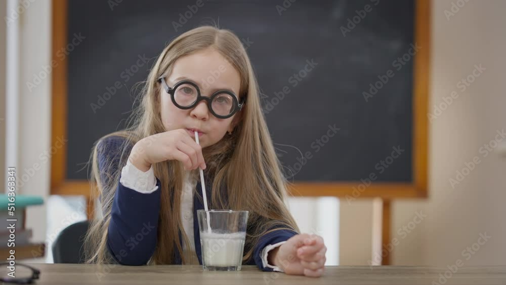 Nerd teen schoolgirl looking at camera drinking milk from glass with ...