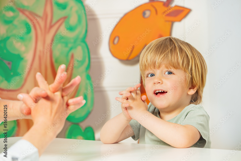 Little blond boy play finger game sitting by the desk in class Stock ...
