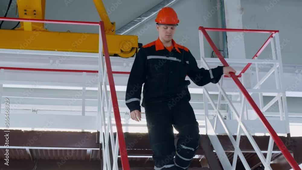 A young worker carefully descends an iron ladder at an oil and gas ...