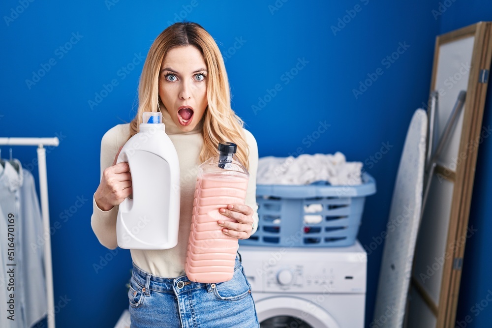 Young caucasian doctor woman holding detergent bottle at laundry room afraid and shocked with ...