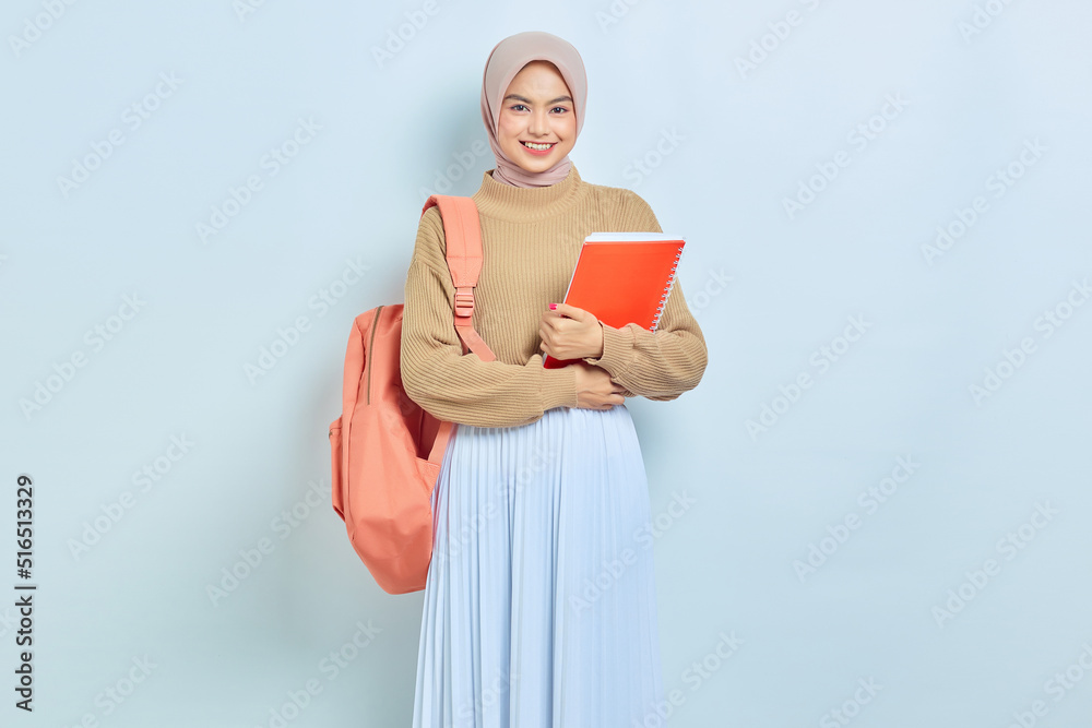 Smiling young Asian Muslim woman student in brown sweater and backpack ...