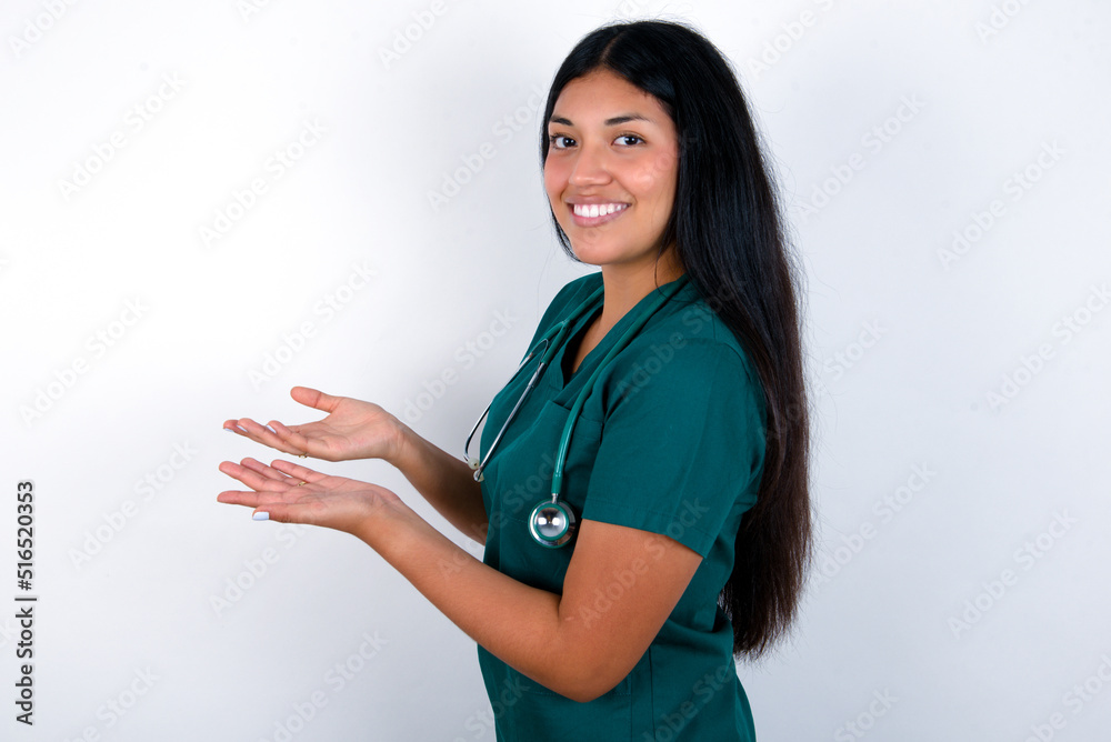 Doctor hispanic woman wearing surgeon uniform over white wall pointing ...