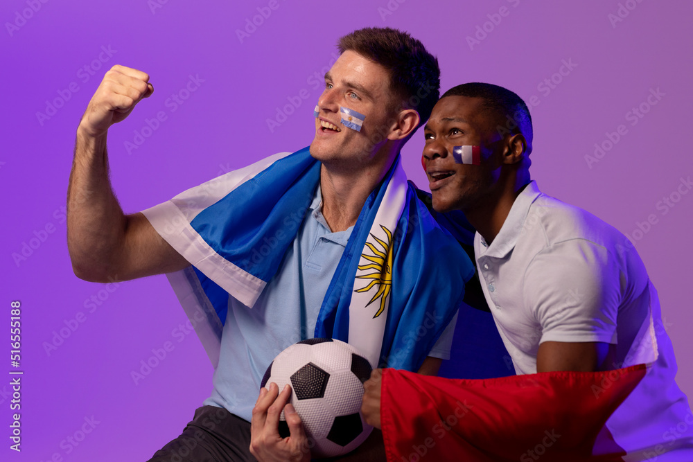 Happy diverse male supporters with national flags over pink lighting ...