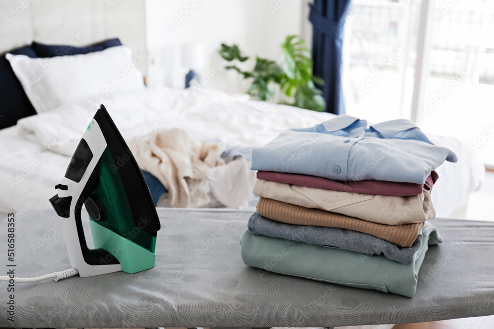 Stack of clean freshly laundered clothes and electric iron on ...