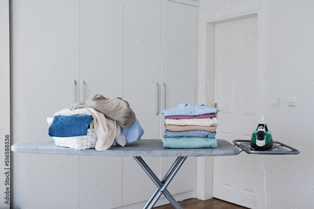 Neat stack of clean freshly laundered clothes and electric iron on ...