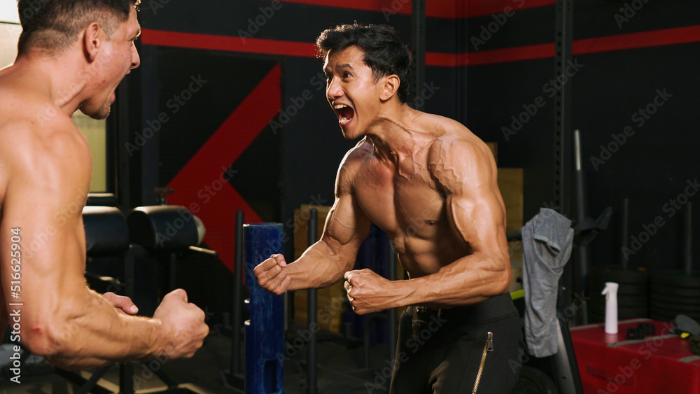 Two multiracial shirtless bodybuilders are shouting and showing ...