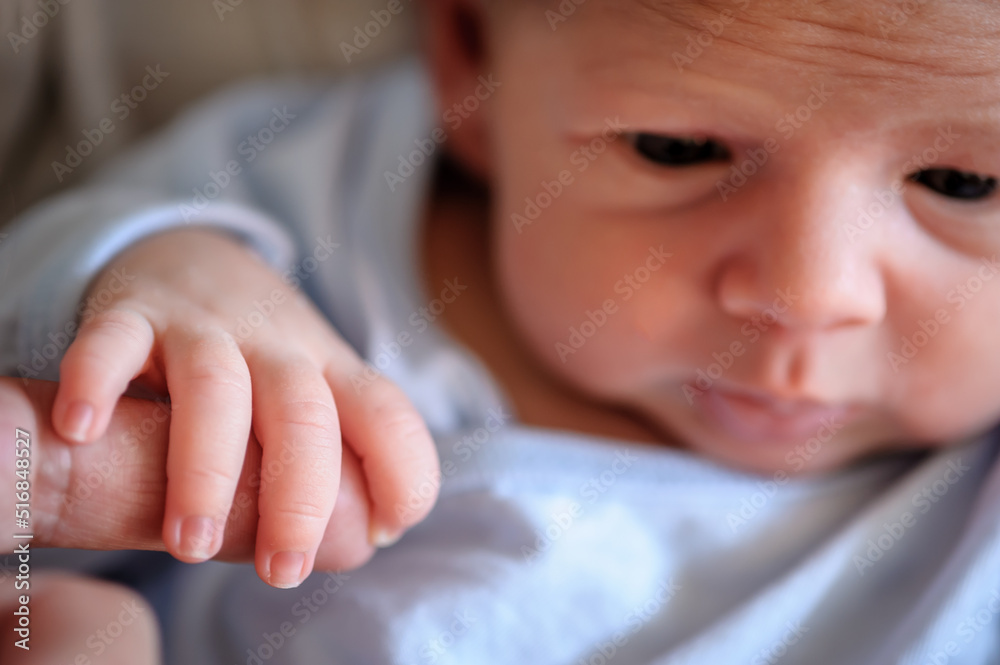 Close-up detail macro view of baby holding on to mom's finger with his ...