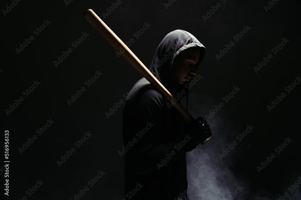 Side view of african american bandit in hood holding wooden baseball ...