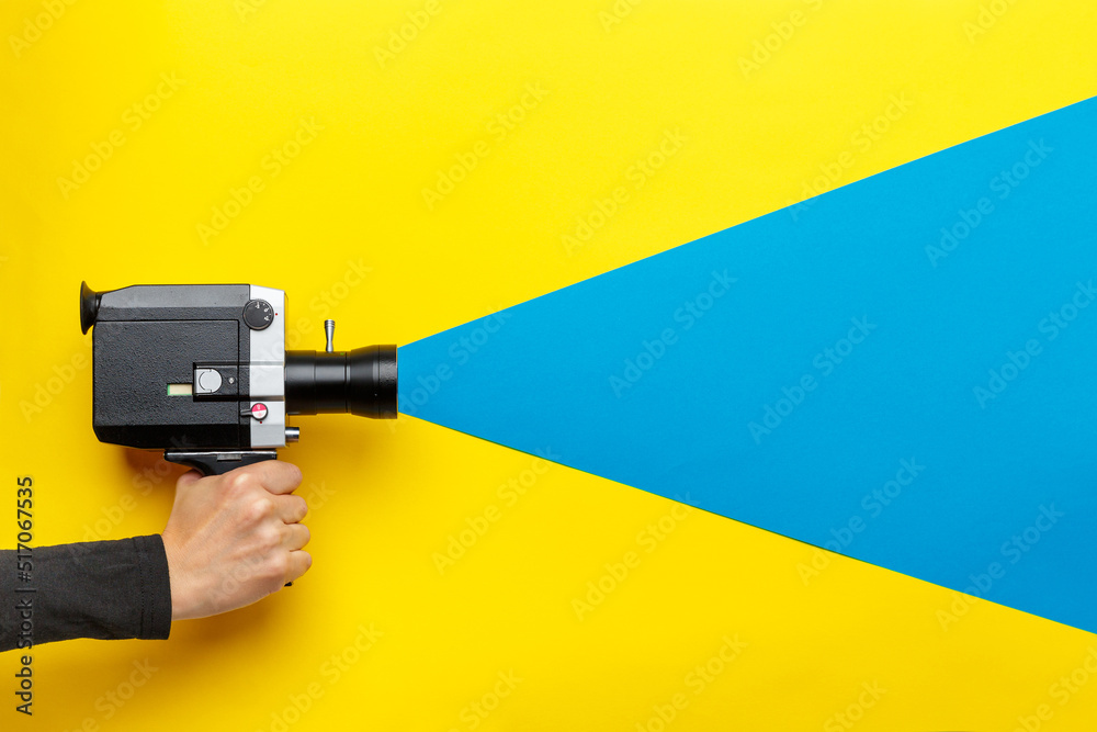 Female hand holding old style film movie camera on a yellow background ...