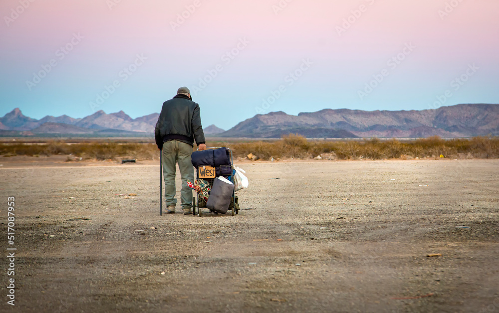 Homeless man walking through the desert with belongings and a sign that ...