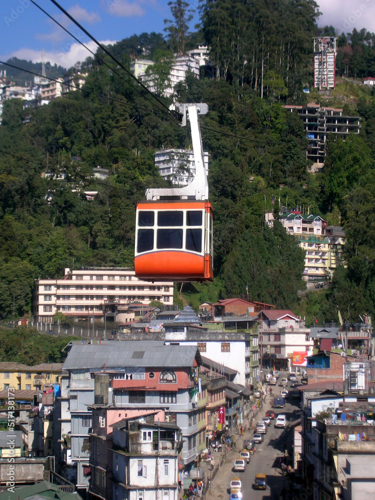 The cable car passing above the houses vehicles on the road looks ...