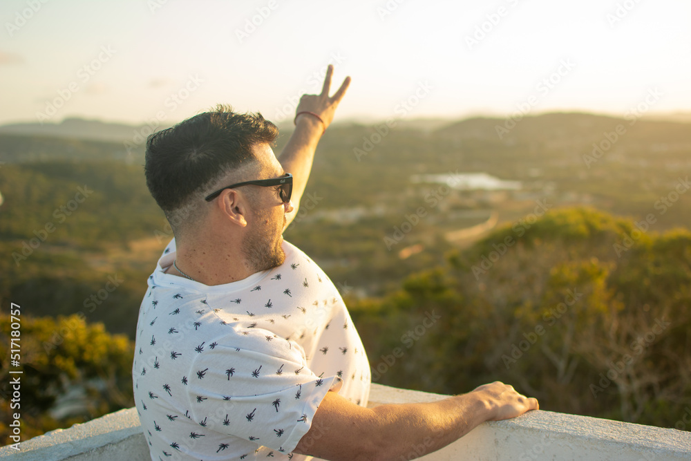 person looking at the cityscape during sunset making the peace symbol ...