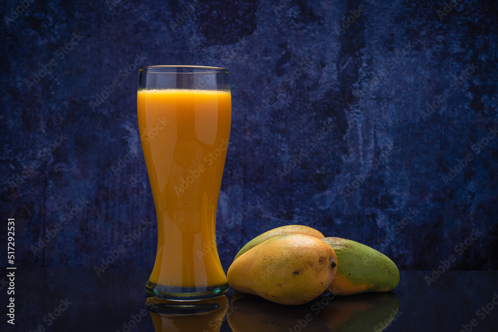 Mango juice glass and group of mangoes on black glass table. Blue ...
