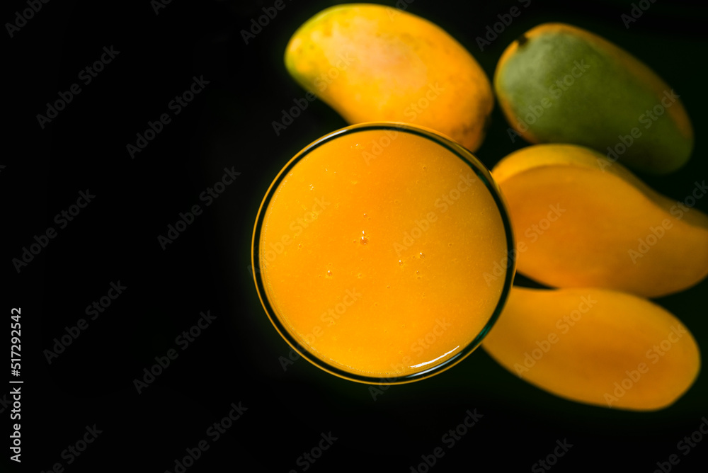 Mango juice glass and group of mangoes on black glass table. Top view ...