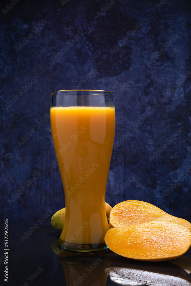 Mango juice glass and group of mangoes on black glass table. Blue ...