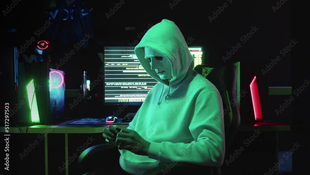 Portrait of a mysterious hacker in a hood, sitting at a table and ...