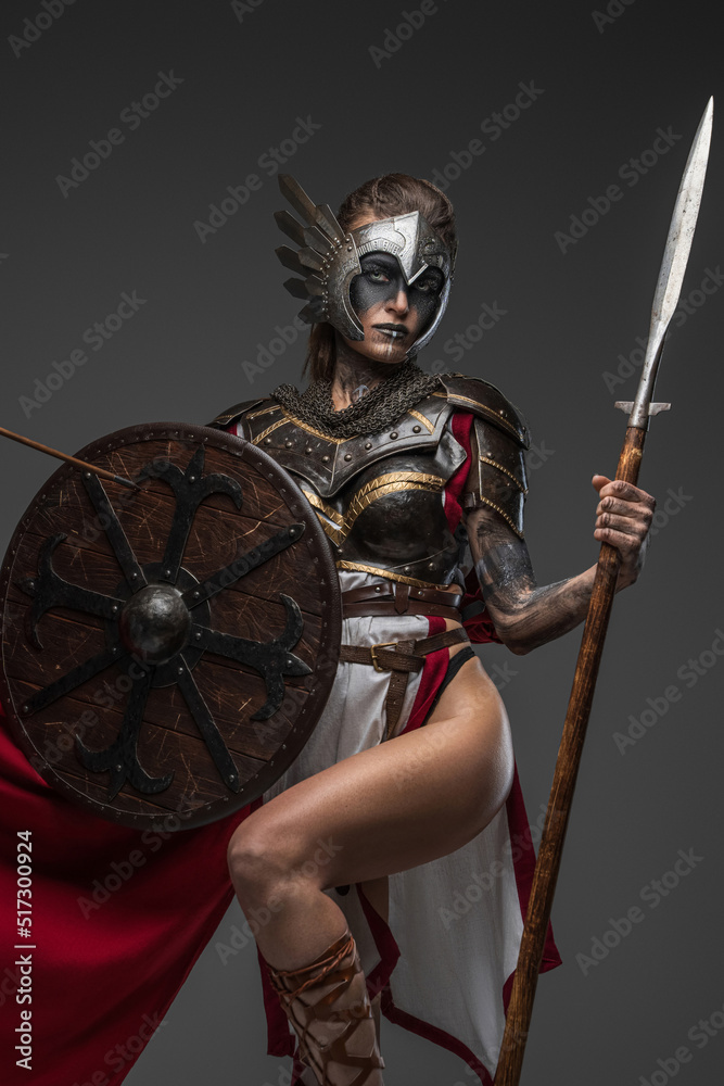 Shot of female warrior from past with shield and spear dressed in armor and red cape looking at ...