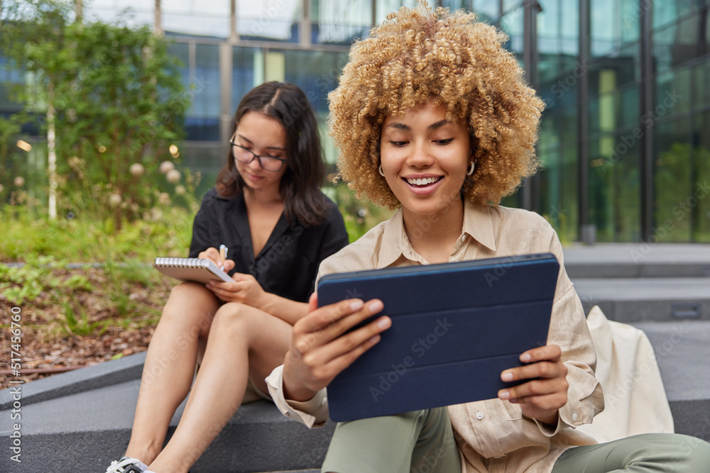 Cheerful curly haired woman uses portable tablet makes photo dressed in ...
