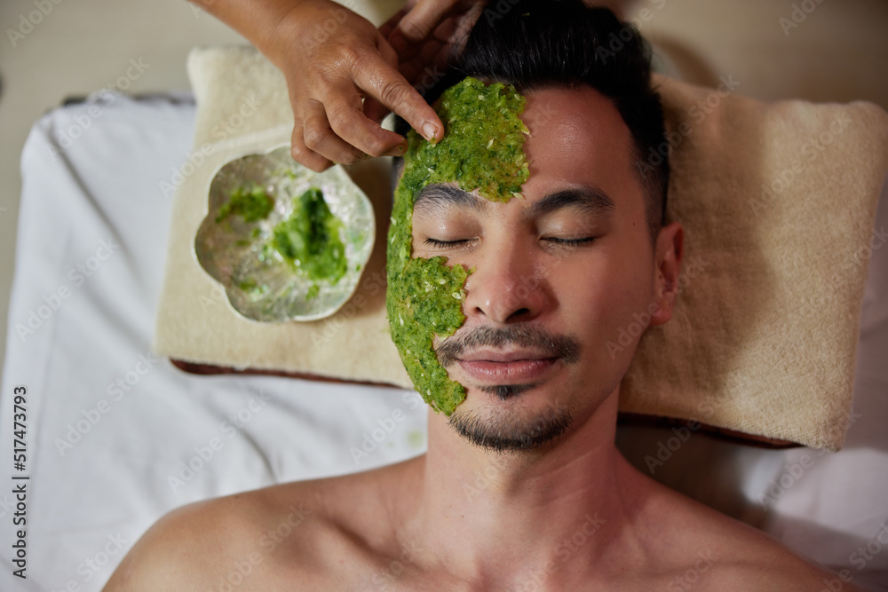 Spa therapist applying fresh cucumber mask on the face of young asian ...