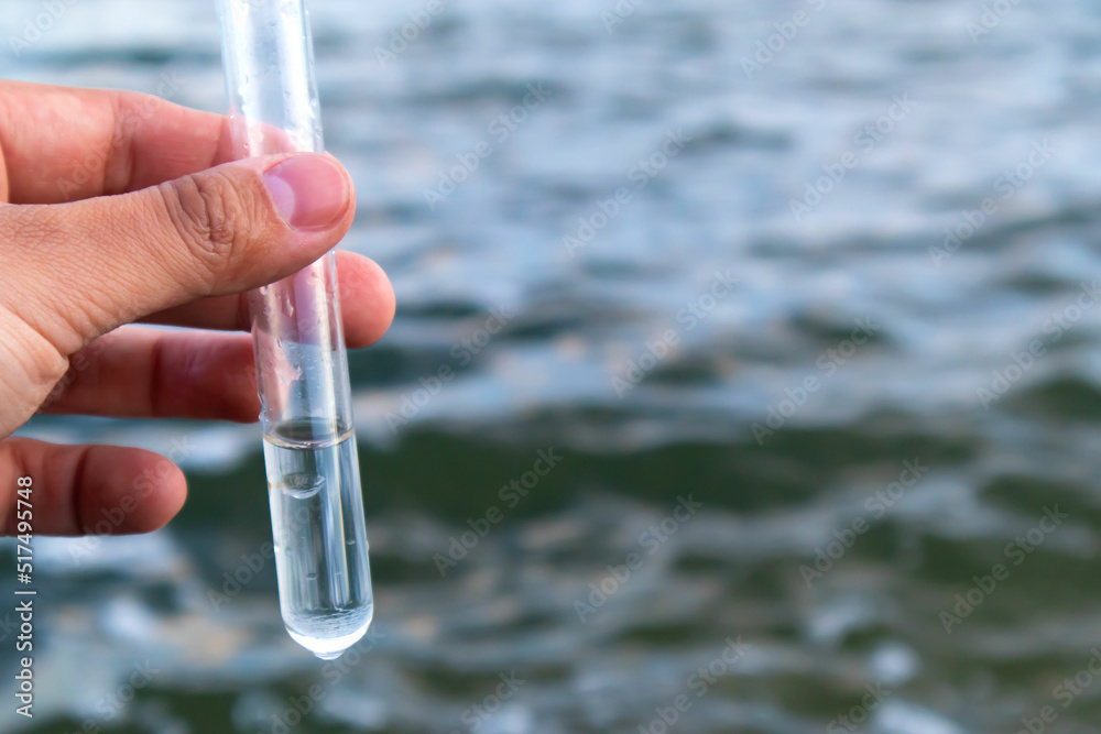 Water sample. Hand holding a test tube with water. Sea in background ...