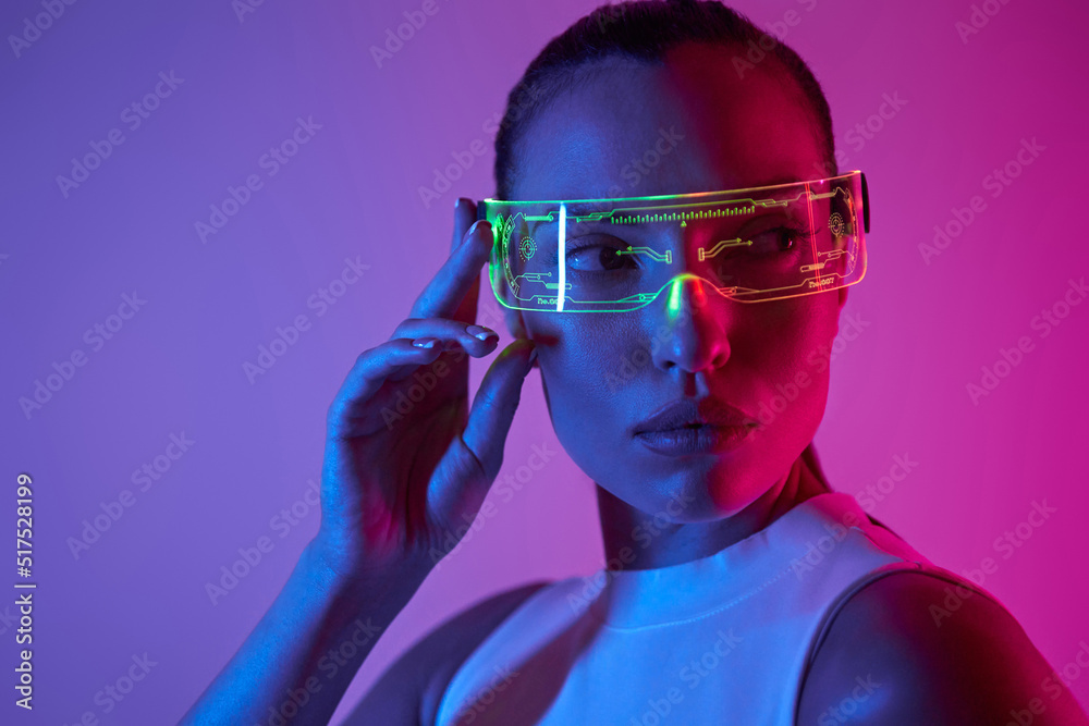 Beautiful young woman adjusting futuristic glasses against dark ...