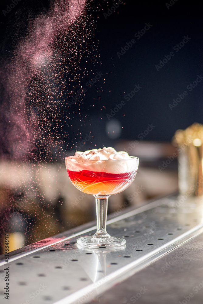 Cocktail with red juice and white foam from whipped cream is sprinkled ...