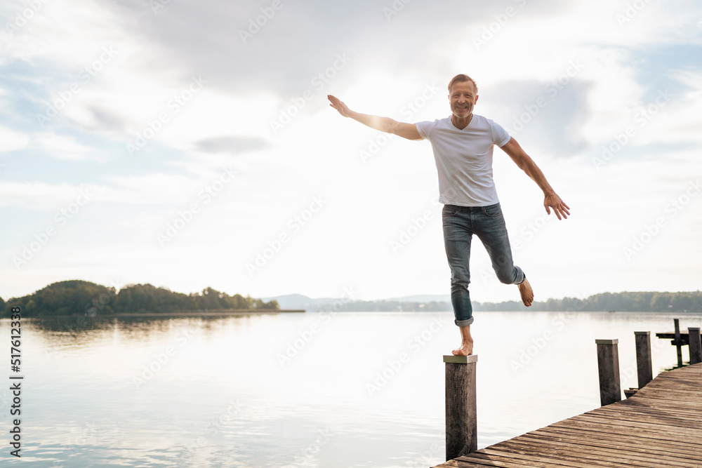 Happy mature man balancing on wooden post of pier Stock Photo | Adobe Stock