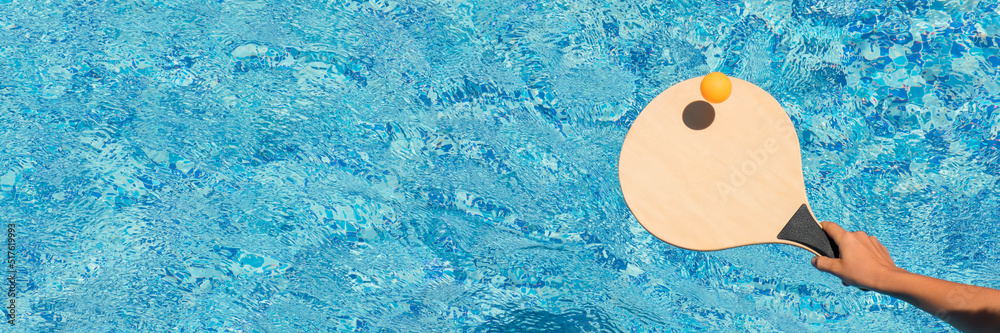 Beach tennis racket in hand of child and ball on blue water background ...