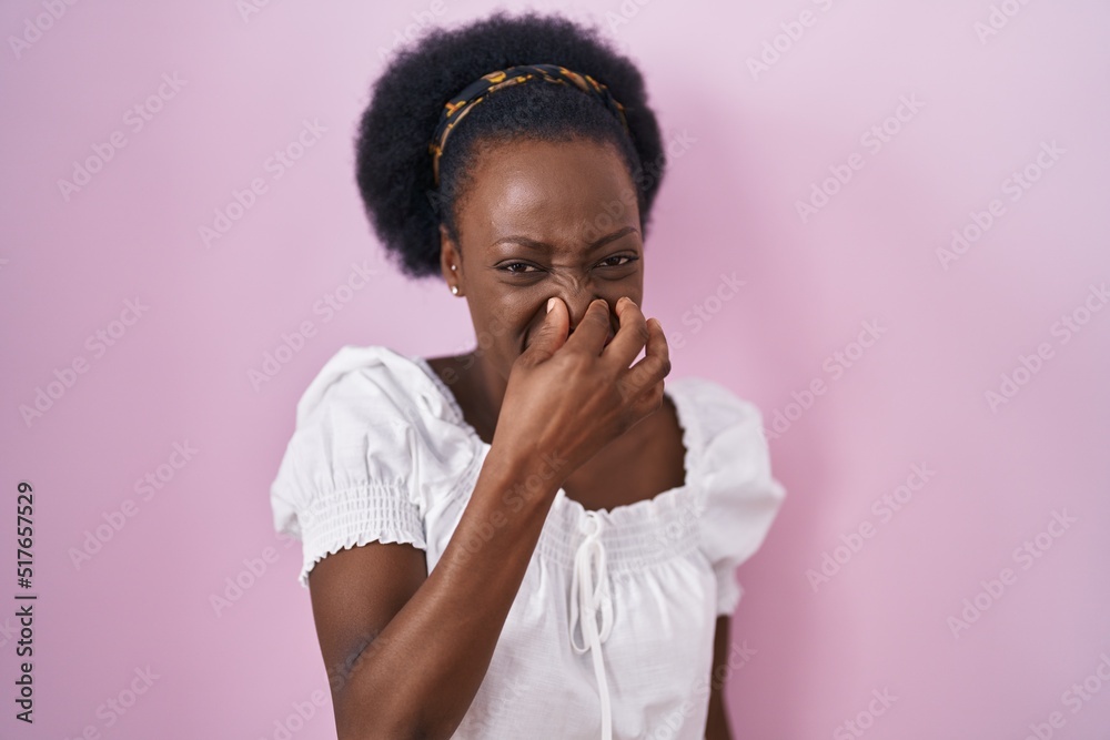 African woman with curly hair standing over pink background smelling ...