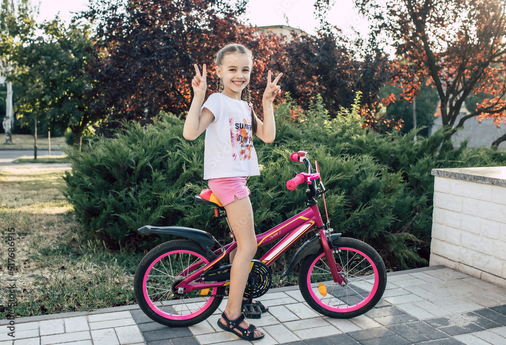The girl child is dressed in summer clothes and rides a red bicycle ...