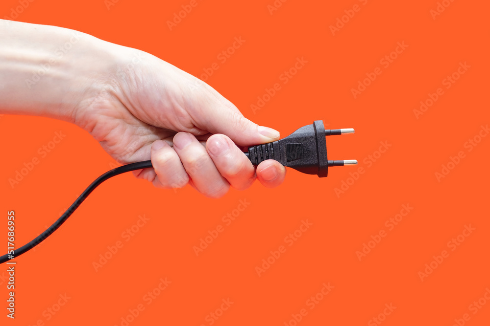 Electric plug for a socket in a hand on an orange background. The ...