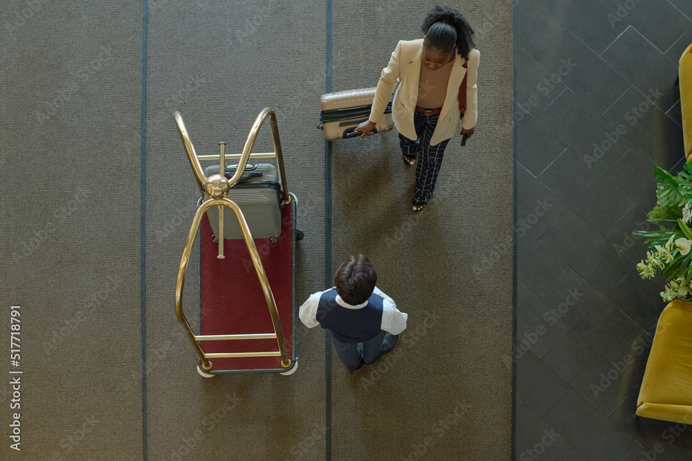 Above shot of young black woman with suitcase moving towards bellboy ...