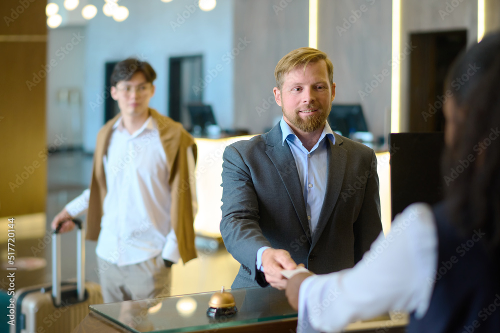 Young smiling businessman giving keycard back to female receptionist by ...
