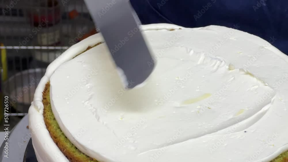 Pastry chef using spatula to frost a smooth cake with buttercream ...