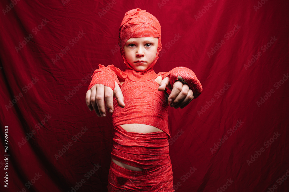 Cute little kid in mummy costume shouting and gesturing in red studio ...